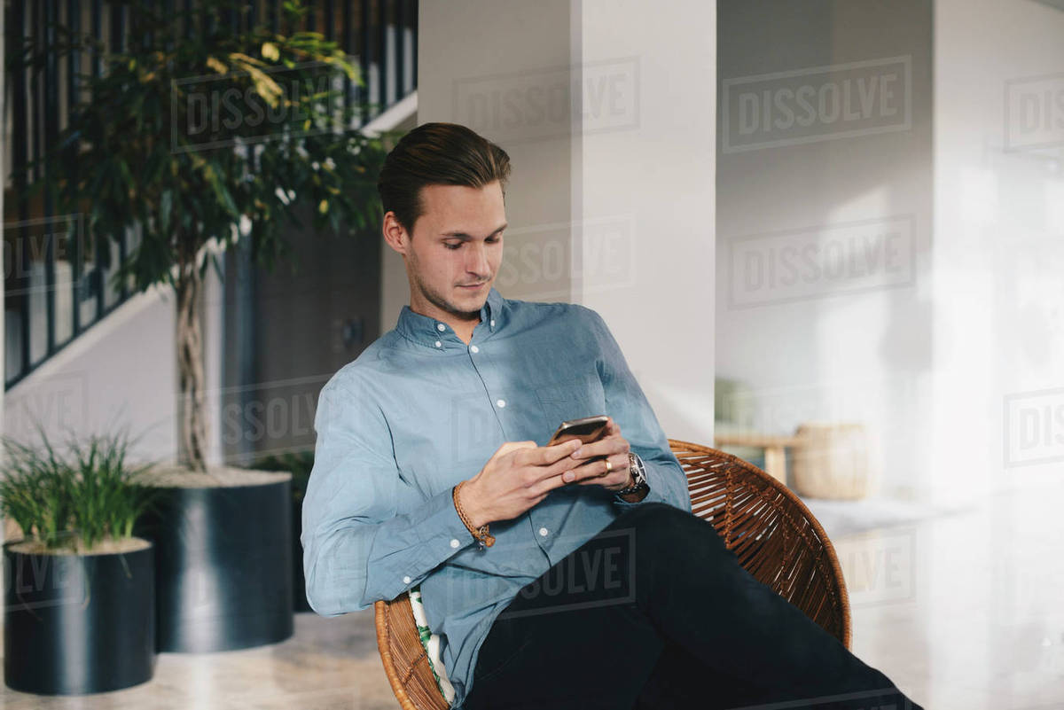 Businessman using smart phone while sitting on chair in office ...