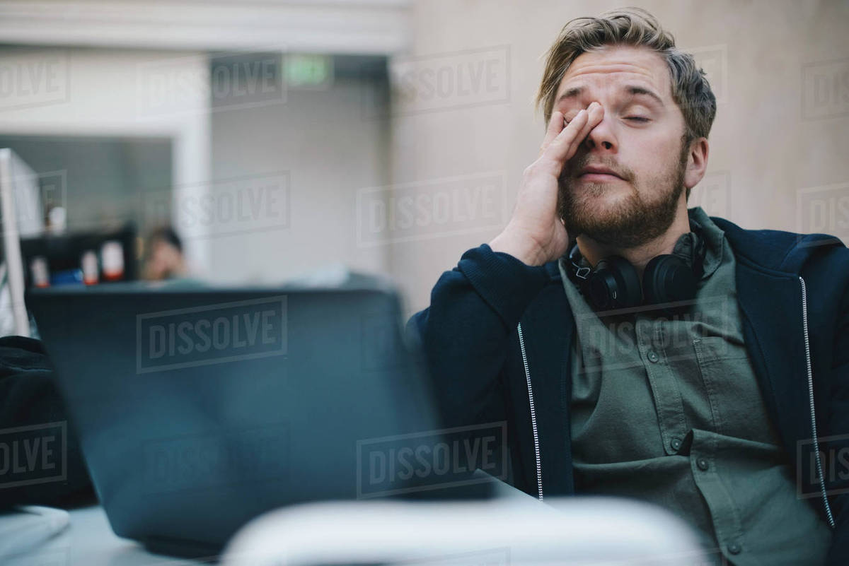 Tired computer programmer rubbing eyes while sitting in office ...