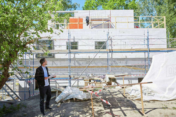 Full length of architect with blueprint looking at incomplete building ...