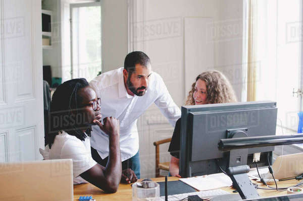 Business people discussing over computer at table in creative office ...