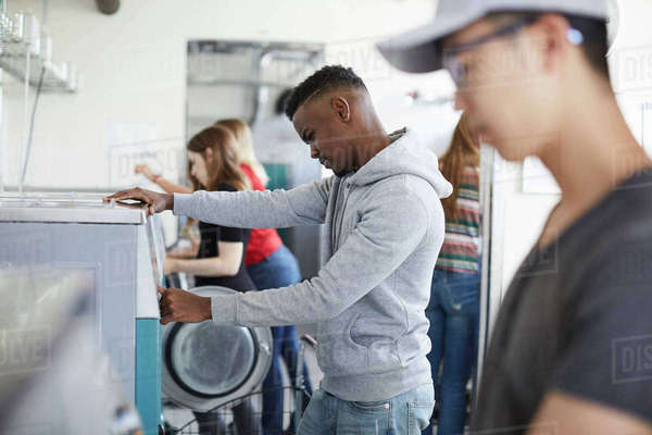 Male and female university students using washing machine at laundromat ...