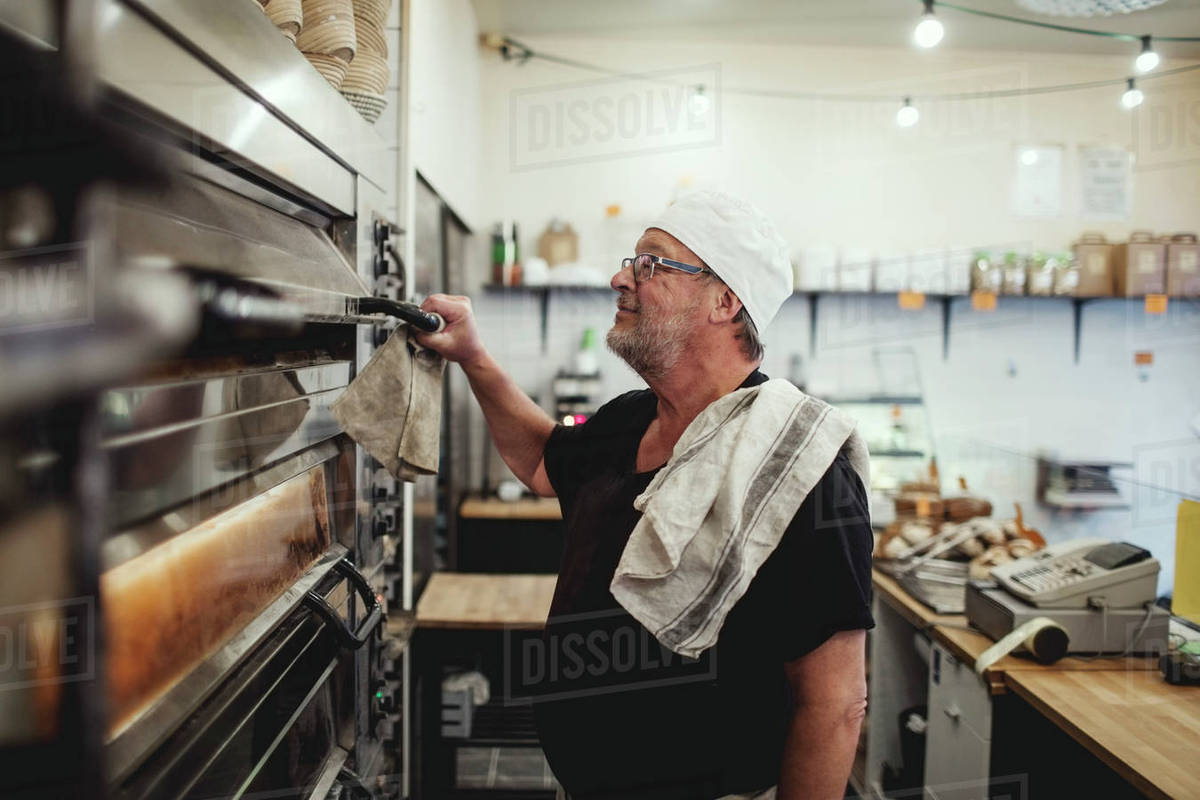 Senior baker standing by oven at bakery - Stock Photo - Dissolve
