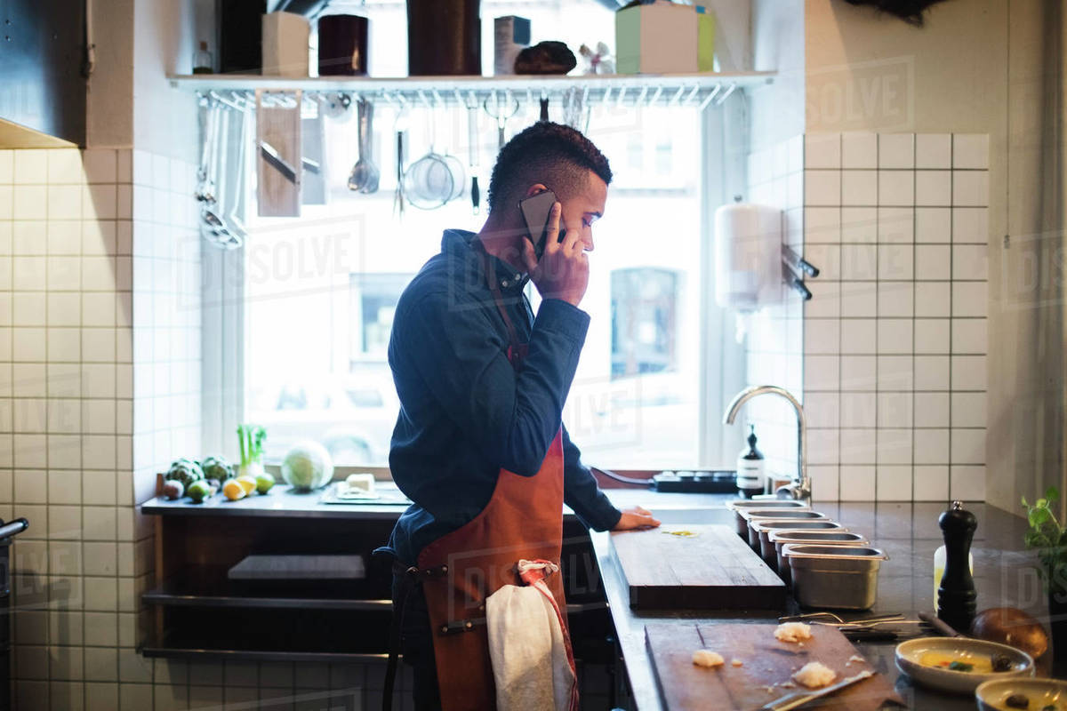 Side view of mature chef talking on mobile phone while standing at ...