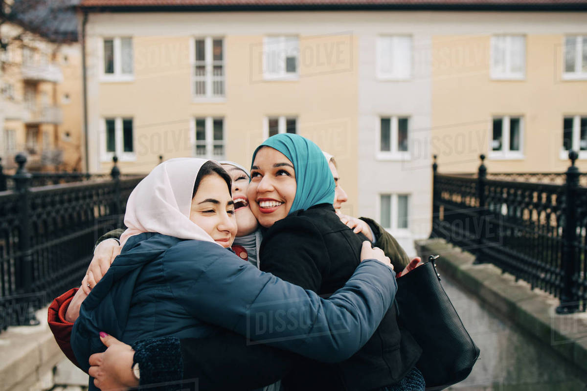 Cheerful multi-ethnic female Muslim friends embracing in city - Royalty ...