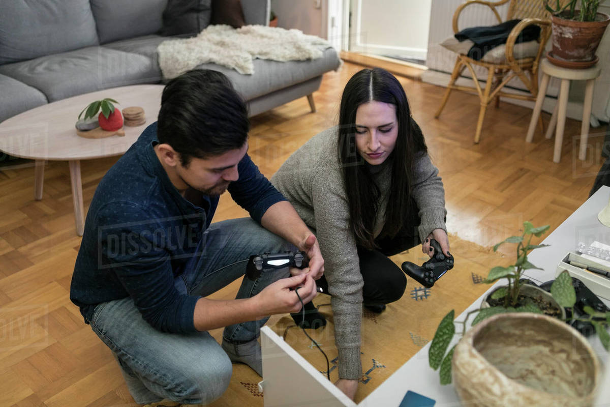 High angle view of couple removing joystick from cabinet in living room ...