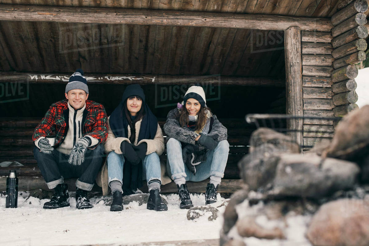 Full length portrait of friends sitting in log cabin against trees ...