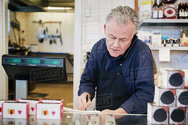Male owner taking order though mobile phone while standing at counter ...
