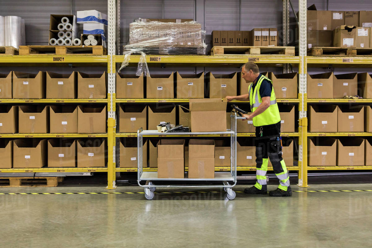 Full length side view of senior male worker pushing cart with cardboard ...