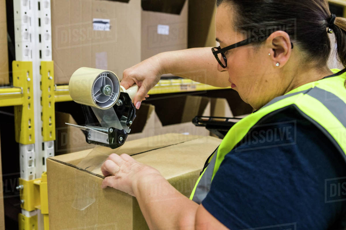 Female worker packing cardboard box with adhesive tape at distribution ...