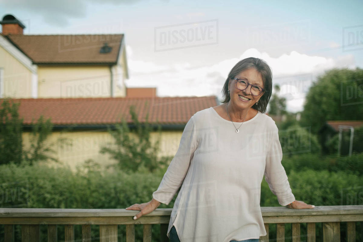Portrait of senior woman standing against railing at porch - Royalty ...