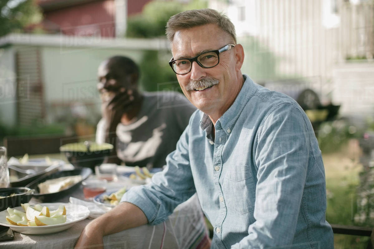 Portrait of smiling senior man sitting at table during garden party ...
