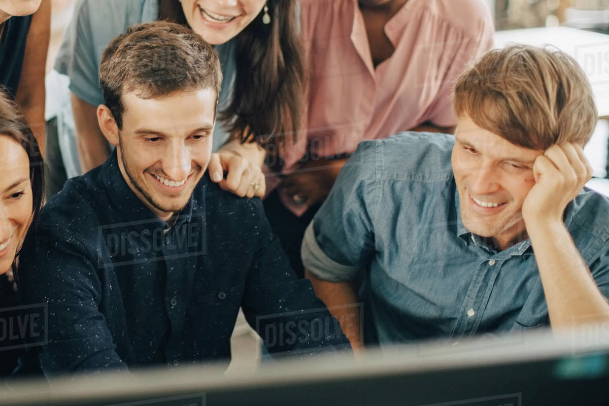 Smiling creative business people looking at computer monitor during ...