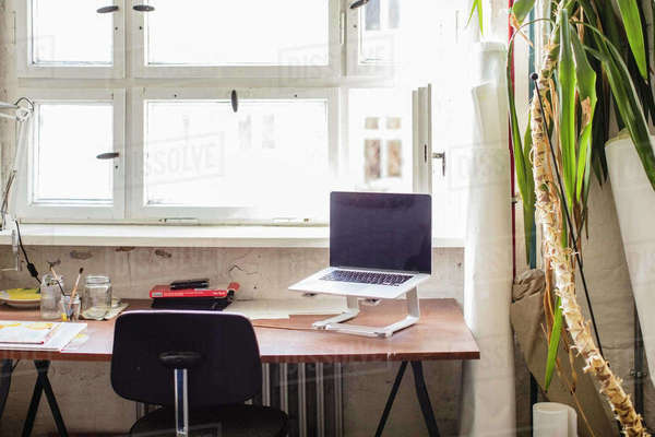 Laptop on stand at desk against window in office - Stock Photo - Dissolve