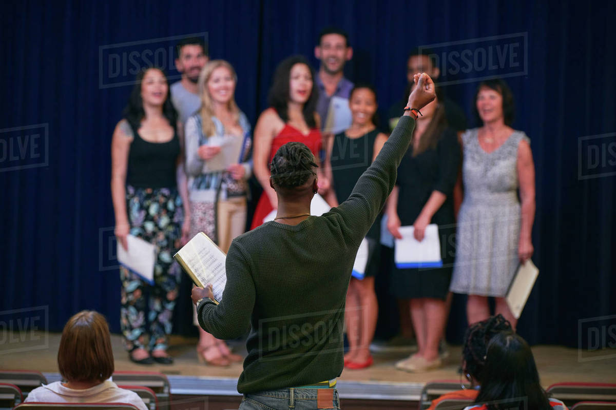 Male conductor with arm raised directing choir in auditorium - Royalty ...