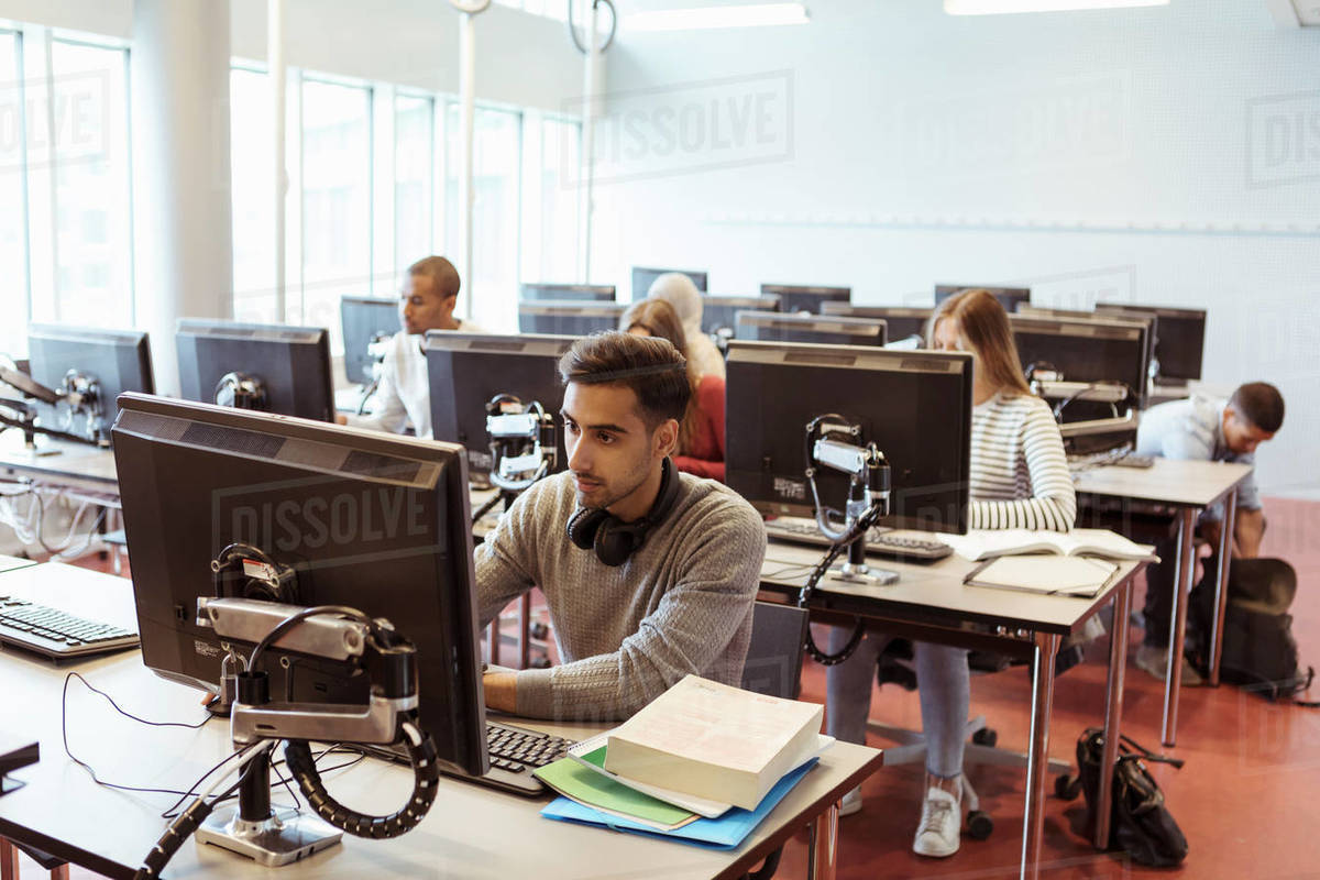 Male and female students using computers at library in university ...