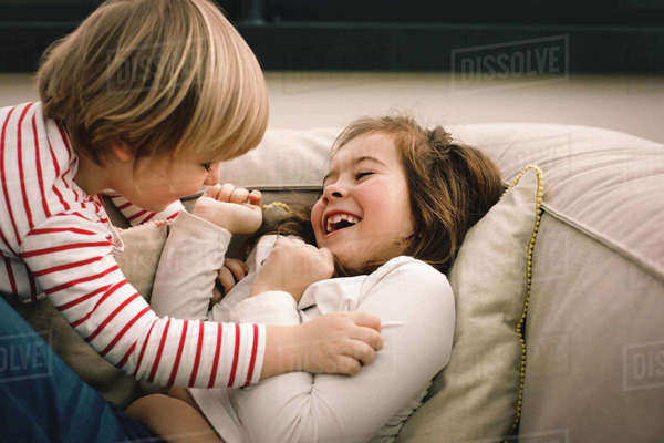 Playful girl tickling cheerful sister on couch at home - Royalty-free ...