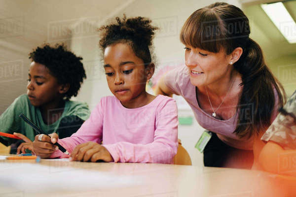 Smiling female teacher looking at students drawing in class - Royalty ...