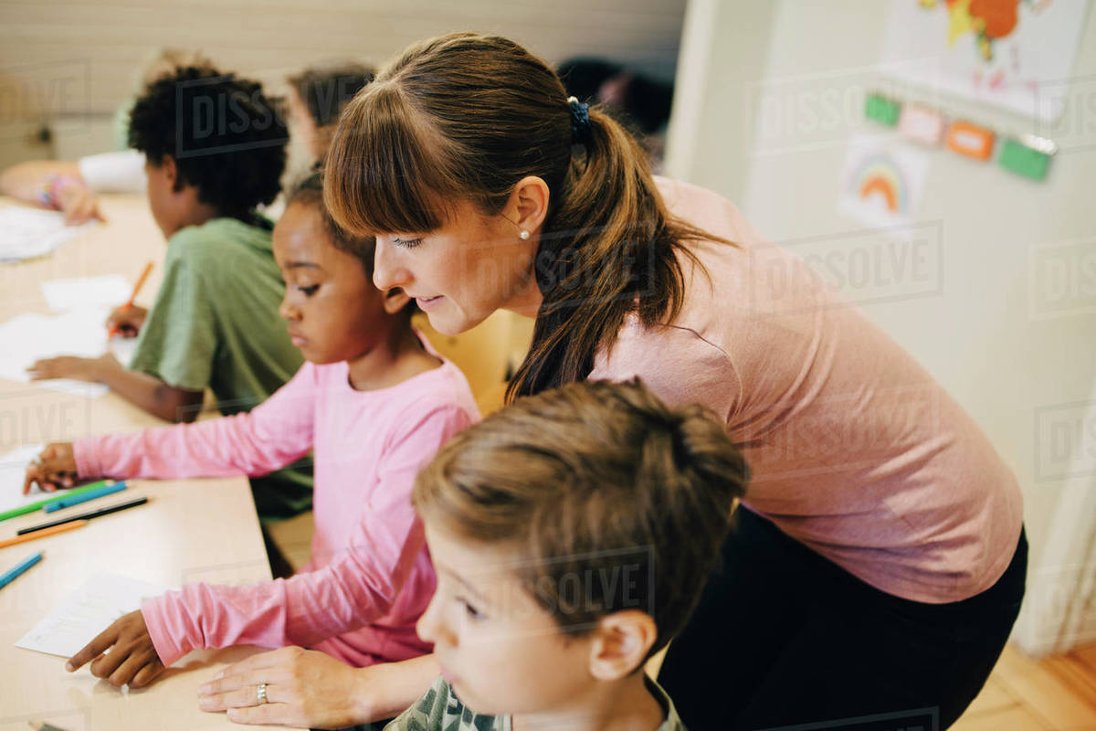 High angle view of teacher guiding students at desk in classroom ...