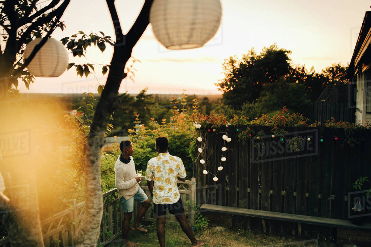 Full length of friends talking while standing in balcony against sky ...