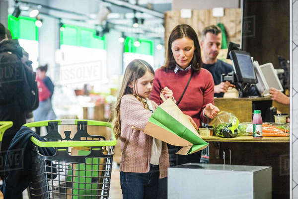 Daughter holding paper bag while standing by mother at checkout counter ...