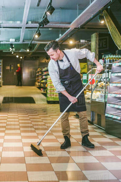 Full length of salesman sweeping floor in grocery store - Stock Photo ...