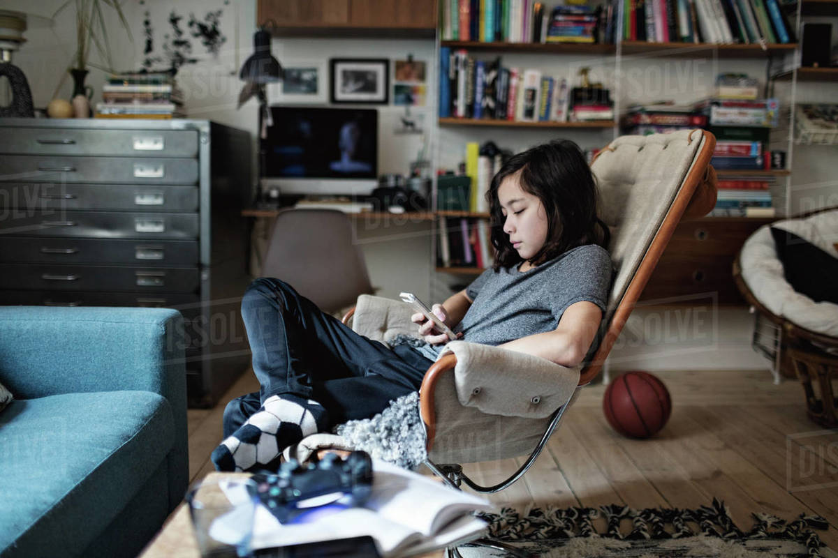 Boy using smart phone while sitting in living room at home - Royalty ...