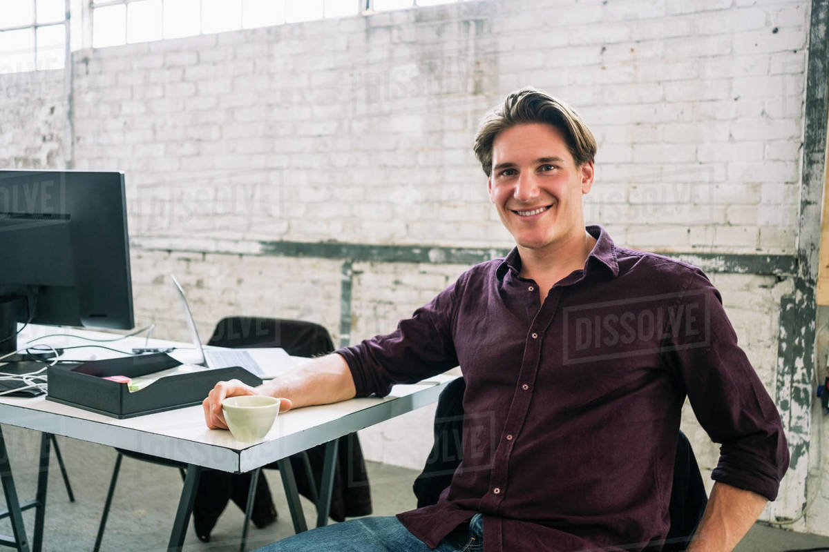 Portrait of confident male IT professional sitting at desk in creative ...