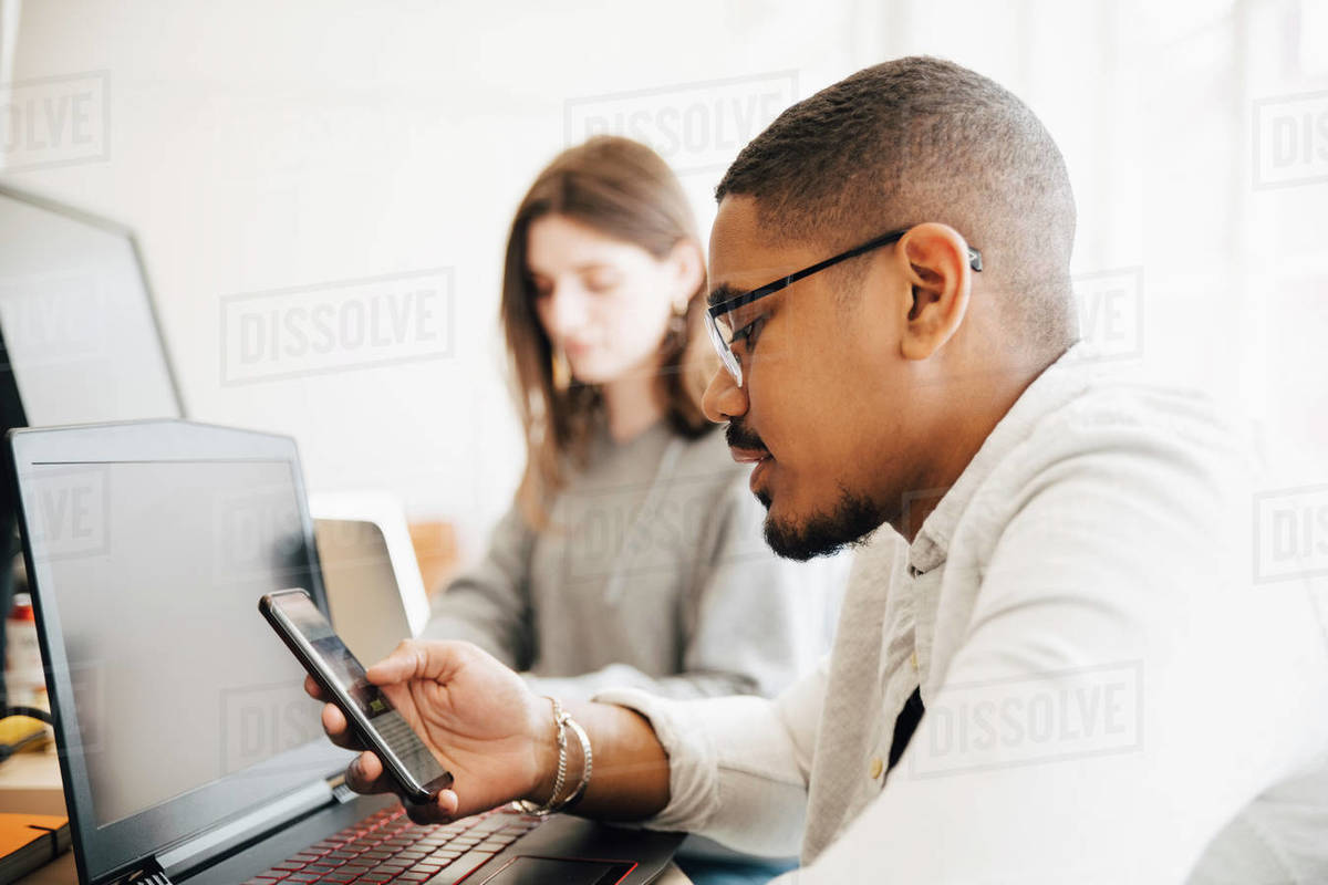 Male computer programmer using smart phone while sitting by female ...