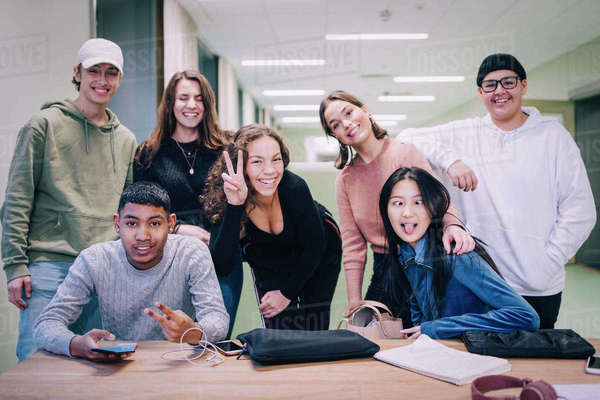 Portrait of teenage classmates making faces at desk in classroom ...