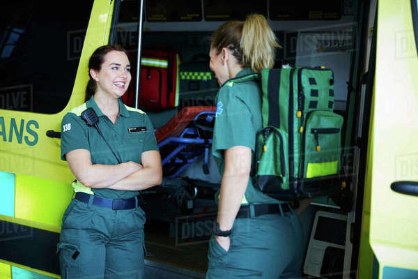 Smiling female paramedics talking while standing by ambulance in ...