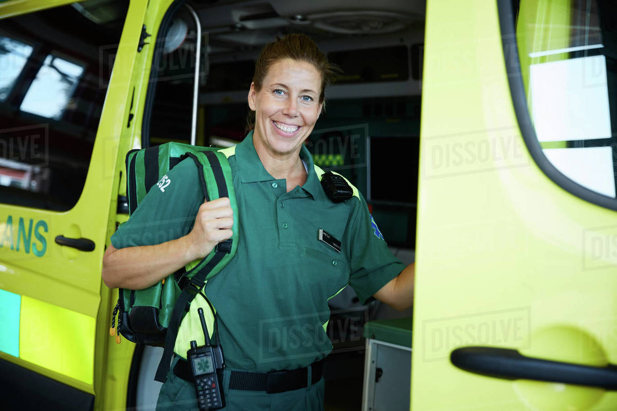 Portrait of smiling paramedic standing outside ambulance in parking lot ...