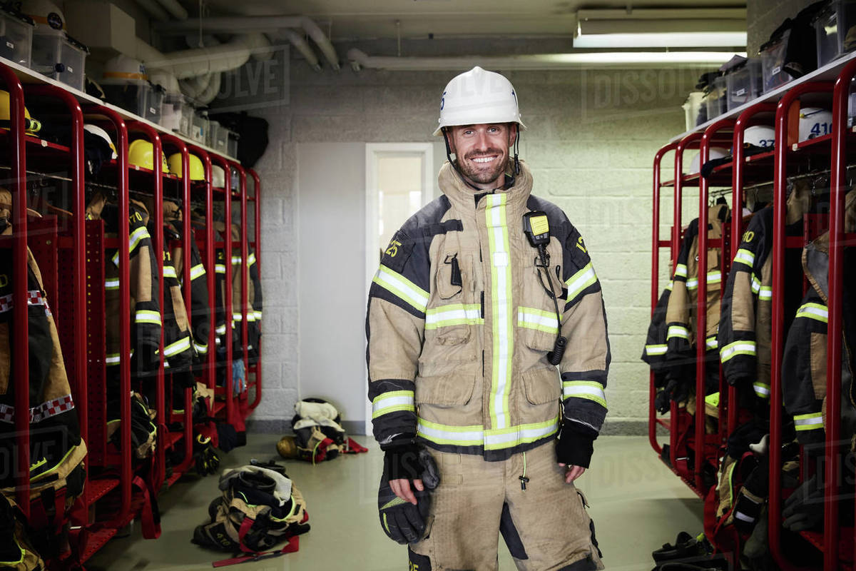 Portrait of smiling male firefighter standing in locker room at fire ...