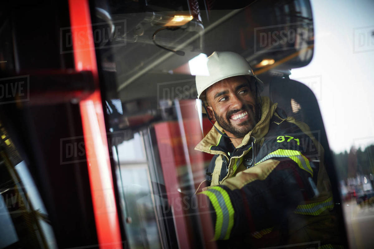 Smiling firefighter sitting in fire engine seen through glass window ...