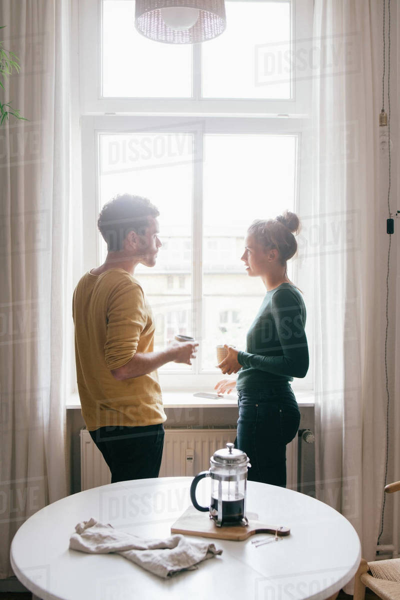 Side view of couple talking while standing by window at home - Royalty ...