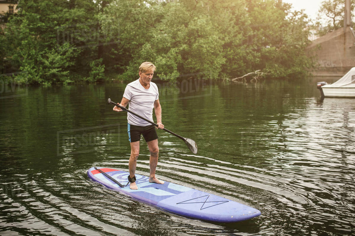 Full length of senior man paddleboarding in sea during SUP course ...