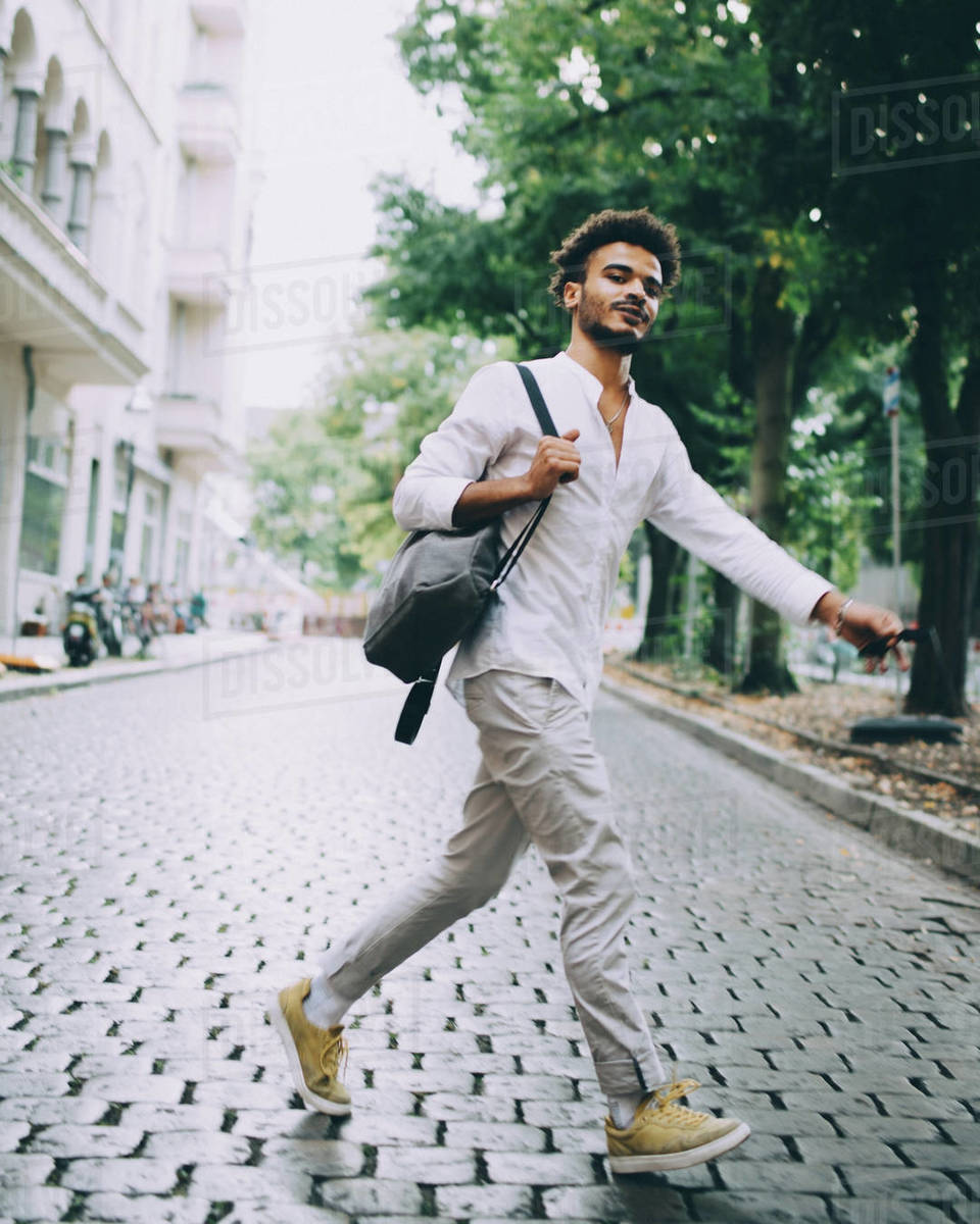 Full length of young man carrying backpack while walking on cobbled ...