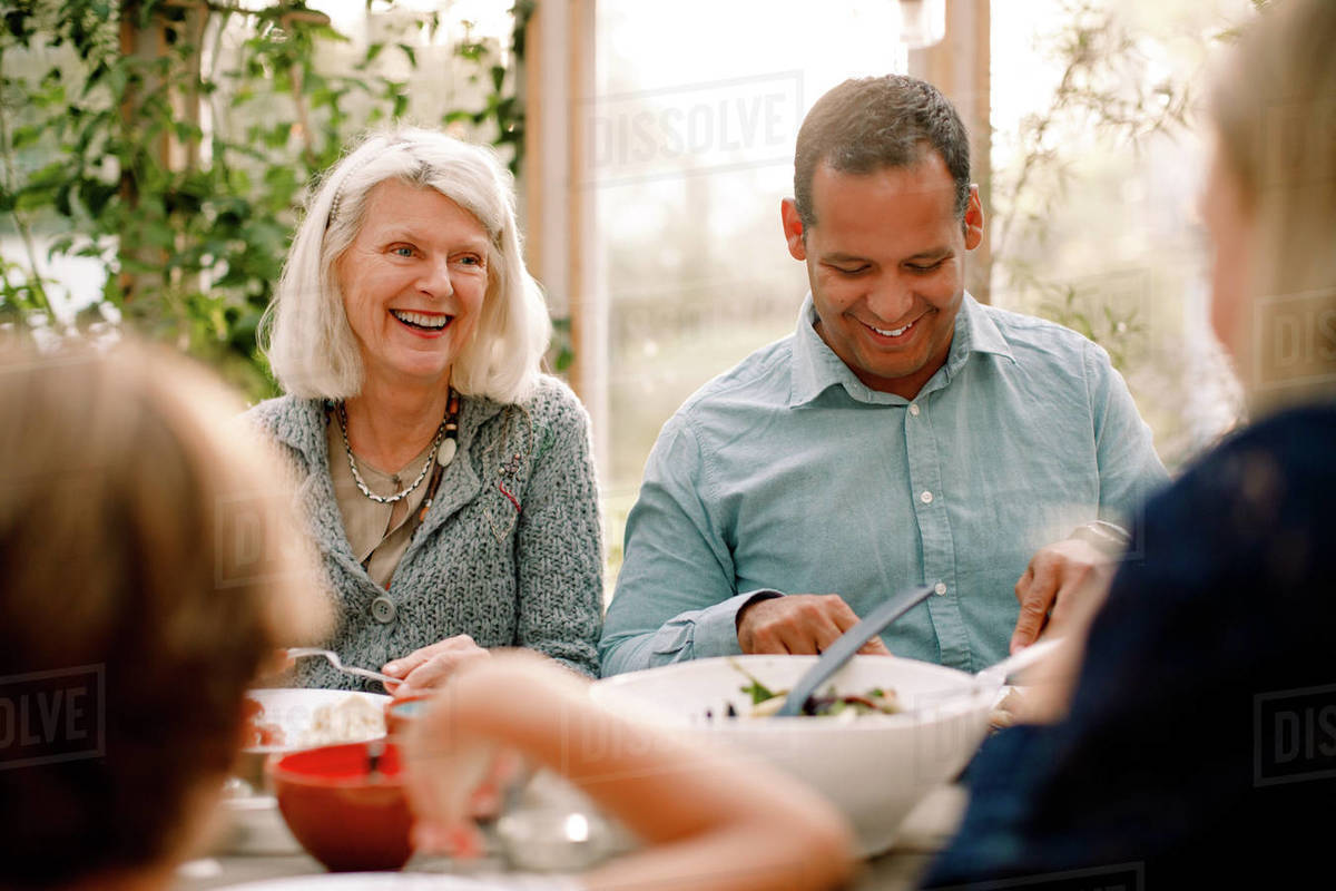 Smiling family enjoying meal while sitting at dining table during lunch ...
