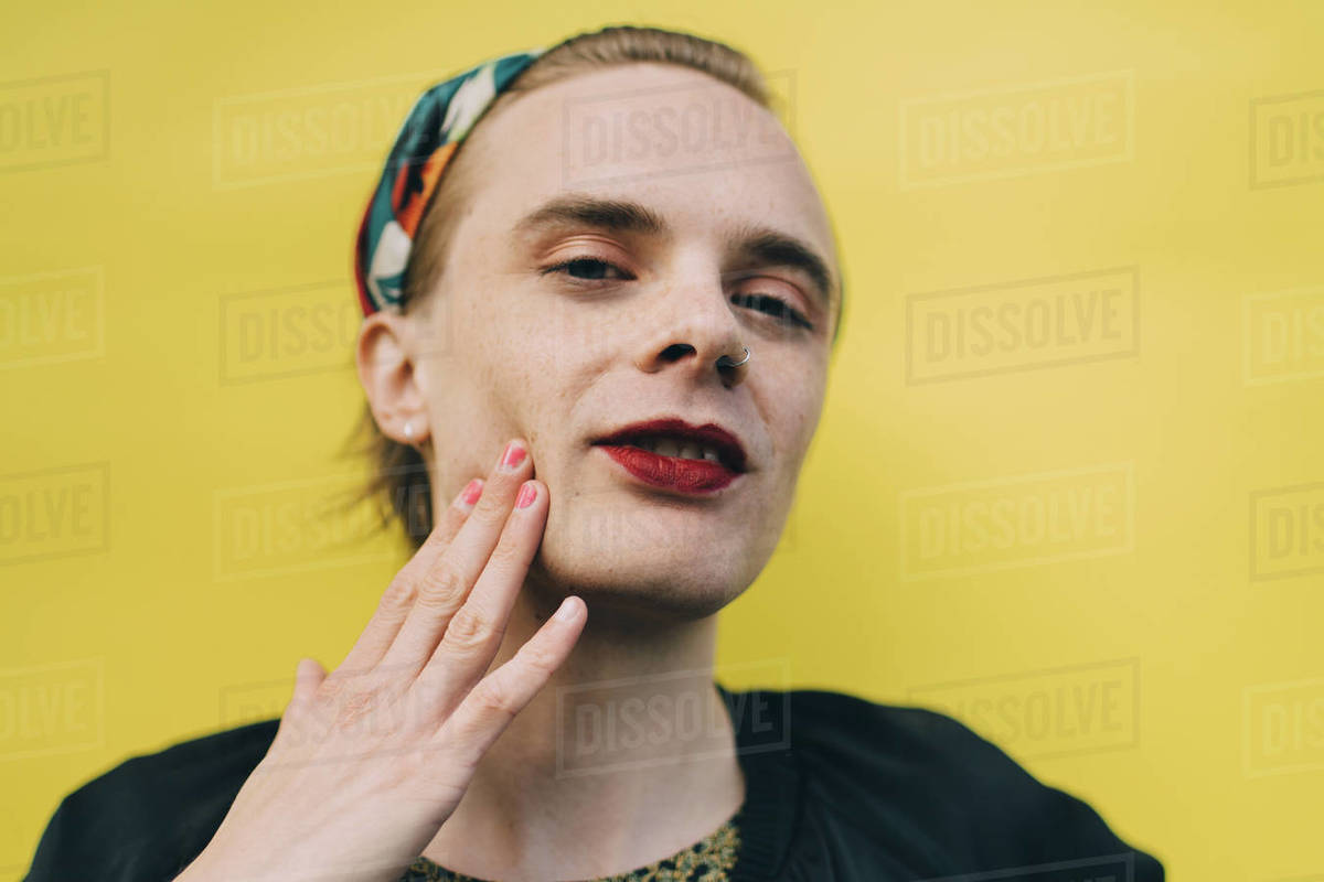 Portrait of smiling man touching cheek while standing against yellow ...
