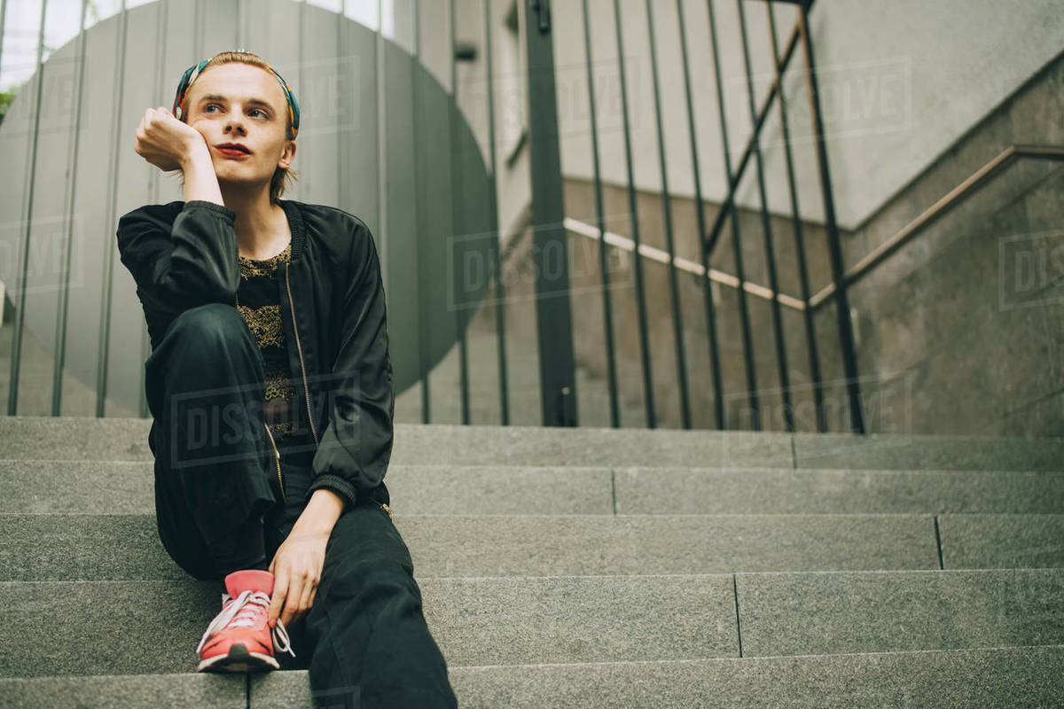 Contemplating young man looking away while sitting on steps - Royalty ...