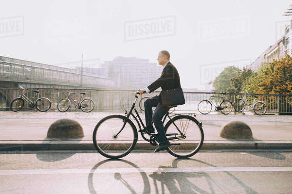 Side view of businessman riding bicycle on road in city against sky ...