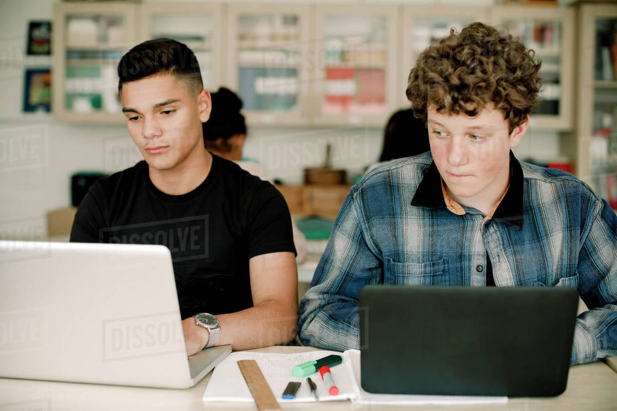 Male students using laptop over table while sitting in classroom ...