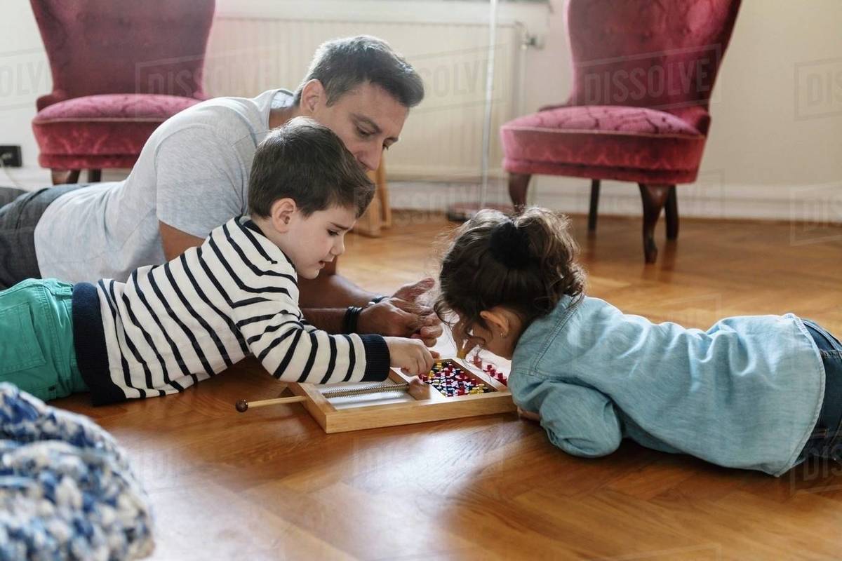 Children playing with toy while lying down with father on hardwood ...