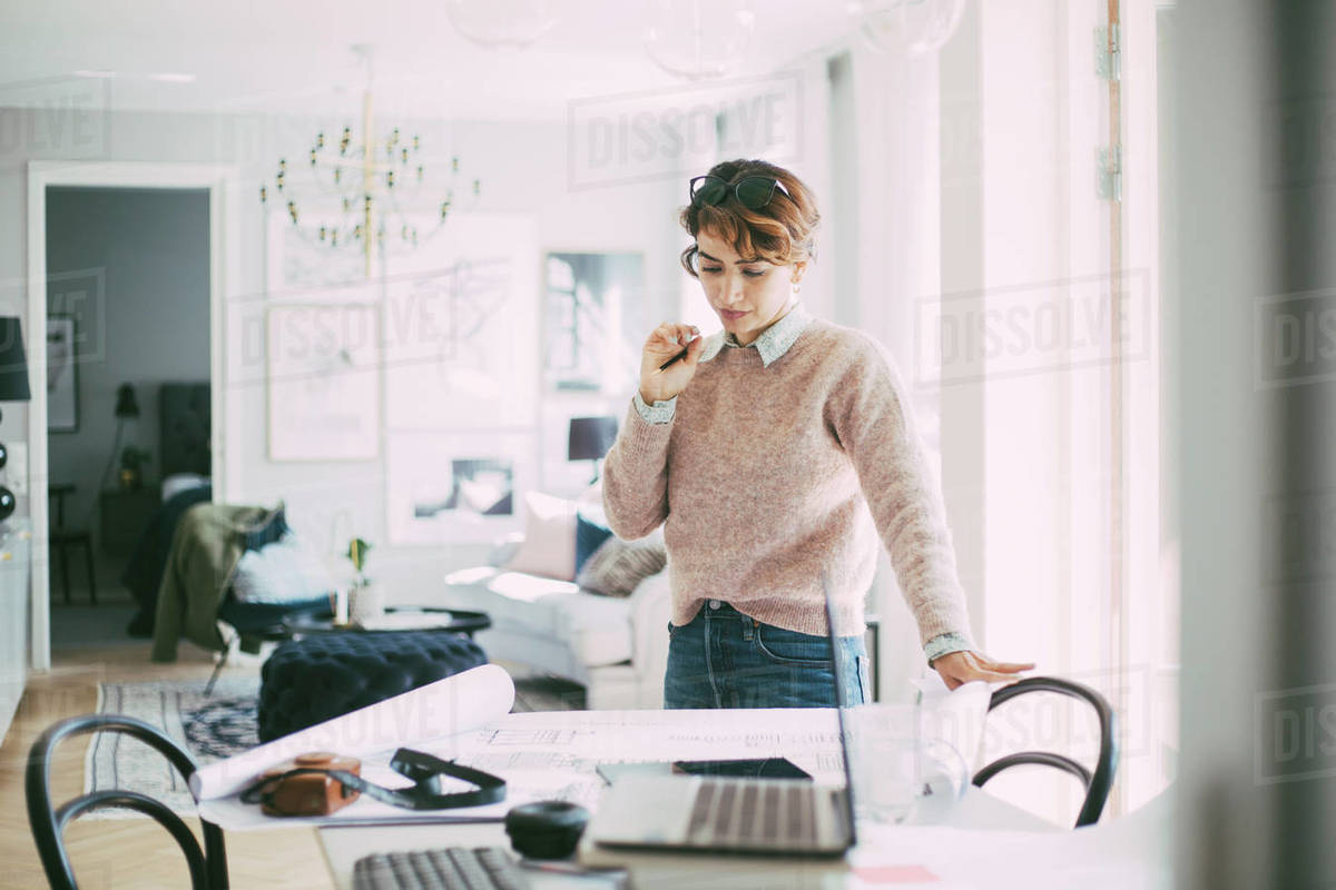Woman standing at table with blueprint working at home - Royalty-free ...