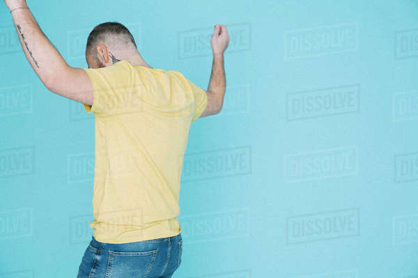 Rear view of man dancing against blue background - Stock Photo - Dissolve
