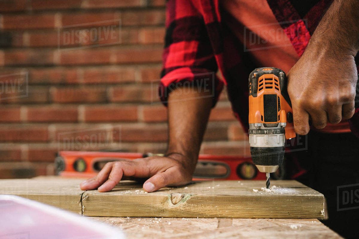 Midsection of man using drill machine on plank while renovating during ...
