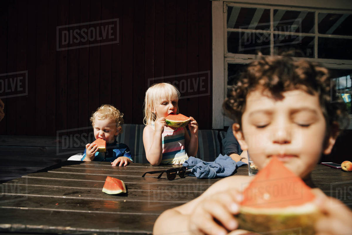 Siblings eating fruit while standing by table during sunny day - Stock ...