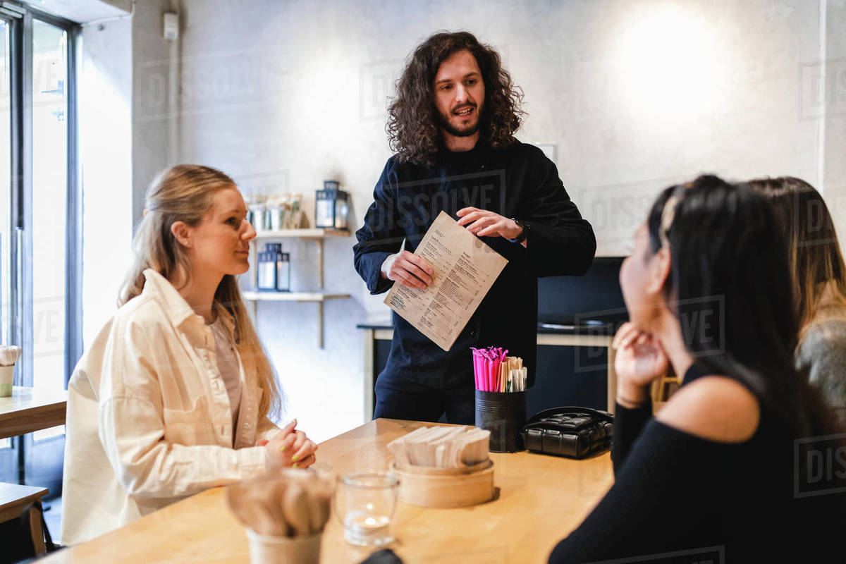 Waiter talking with female customers while taking order in restaurant ...