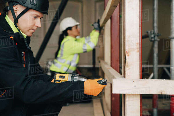 Side view of male worker using drill on wooden plank while working at ...
