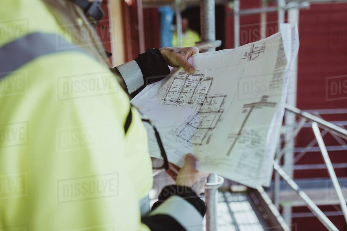 Female building contractor reading floor plan at construction site ...