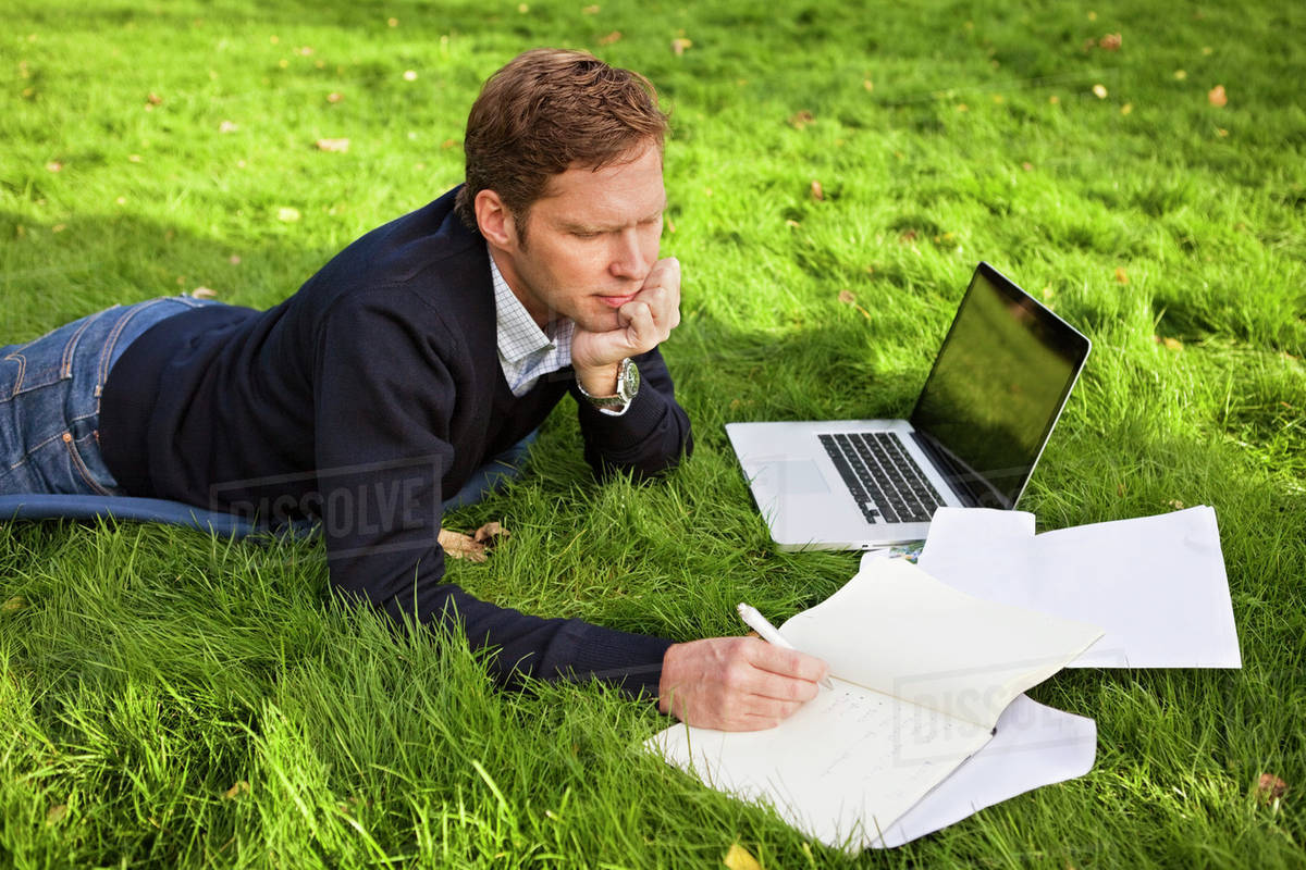 Man laying in grass and write in a book - Stock Photo - Dissolve